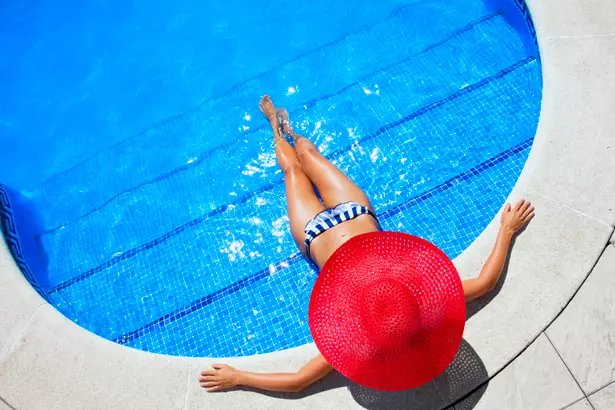 žena s kloboukem proti slunci u bazénu